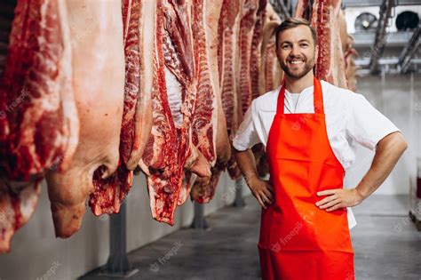 Premium Photo | Young butcher at the meat factory standing by the hanging meat