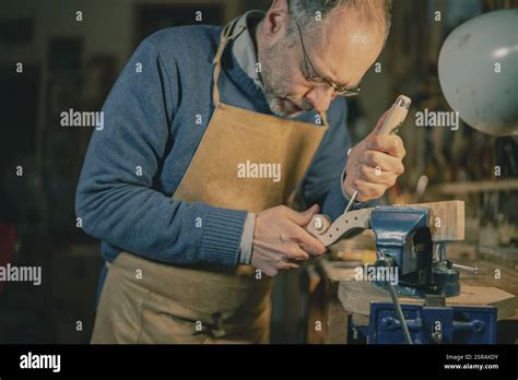 Italian Luthier Carefully Carving A Violin Scroll With A Gouge In A Warmly Lit Workshop