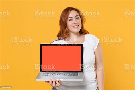 흰색 티셔츠를 입은 젊은 빨간 머리 와 몸긍정적 인 여성 20 대는 노란색 색상 배경 스튜디오 초상화에 고립 된 복사 공간을 모의 빈 빈 화면으로 노트북 Pc 컴퓨터를