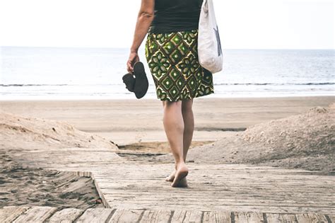 해변과 바다를 향해 소박한 나무 산책맨발로 걷는 트렌디 한 젊은 여성 손에 가죽 샌들을 들고 걷는 소녀의 뒷모습 여름 휴가 및