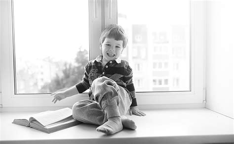 그 어린 소년이 책을 읽고 있습니다 아이는 창가에 앉아 공과를 준비한다 책을 손에 들고 있는 소년이 창턱에 앉아 있다 겨울에 대한 스톡 사진 및 기타 이미지 Istock