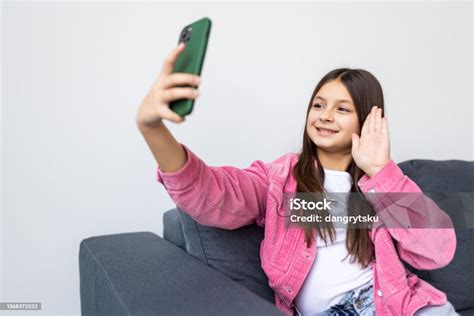매력적인 쾌활한 소녀 인플루언서 블로거의 초상화는 가벼운 평면 집에서 셀카 비디오 스트리밍 자유 시간을 복용 소파에 앉아 Brand Name Smart Phone에 대한