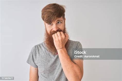 젊은 빨간 머리 아이리쉬 남자 는 입물고 손톱에 손을 가진 스트레스와 긴장 찾고 고립 된 회색 배경 위에 서 티셔츠를 입고 불안 문제 T 셔츠에 대한 스톡 사진 및 기타