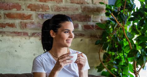 커피 한잔을 가진 아름 다운 젊은 여자입니다 여자는 집에서 일출과 함께 아침에 신선한 커피를 즐깁니다 아침에 커피를 마시는 아름다운 여자 창가에 앉아 사진