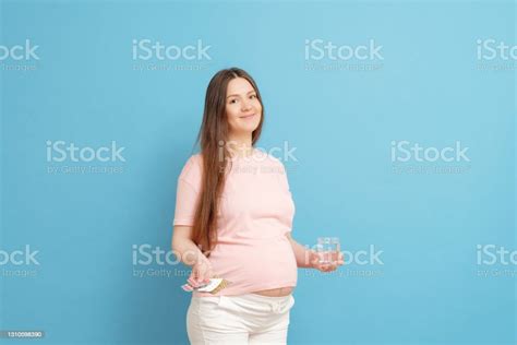 푸른 배경에 젊은 아름다운 임신 한 여자는 그녀의 손에 알약을 잡고 물 한 잔 개념에 대한 스톡 사진 및 기타 이미지 개념