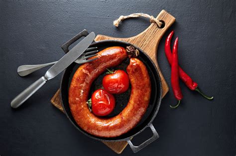 어두운 돌 테이블 위의 나무 도마에 토마토 고추 수저를 곁들인 주철 팬에 튀긴 돼지고기 소시지 0명에 대한 스톡 사진 및 기타 이미지 Istock