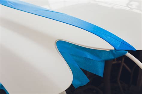 작업 하는 동안 자동차 수리 노동자 차량 수리 워크샵에서 도장 하는 동안 페인트로 채우지 않기 위해 접착 테이프로 흰색의 몸체 요소의 일부를 붙여 넣습니다 0명에 대한 스톡