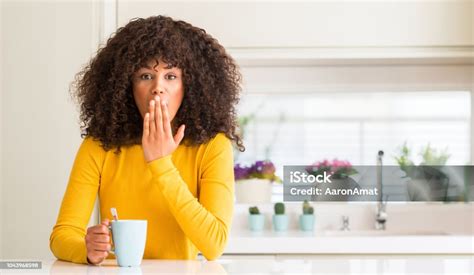 아름 다운 아프리카계 미국인 여 자가 손으로 커버 입 실수 두려움의 표현에 대 한 수치와 충격 집에서 커피 한 잔을 들고 침묵 비밀 개념에에서 무서 워 가리기에 대한 스톡