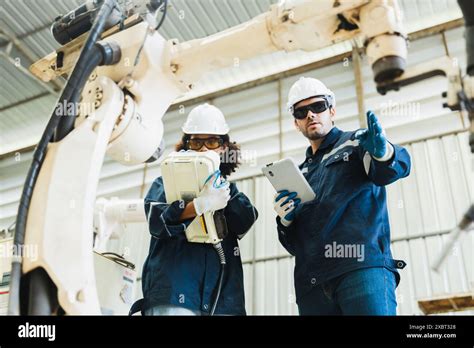 Engineer Controlling Robot Arm At Factory Checking The Operation Of