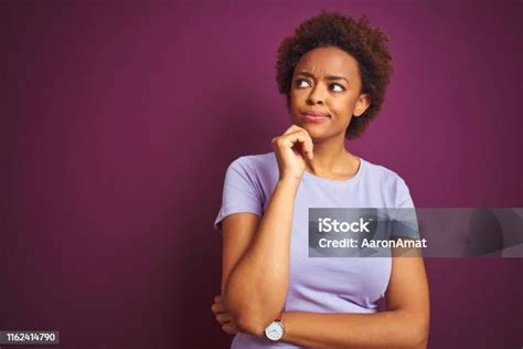 질문 펜심 표현에 대해 생각 턱에 손으로 고립 된 보라색 배경 위에 아프리카 머리를 가진 젊은 아름다운 아프리카 계 미국인 여성 사려 깊은 얼굴로 미소 의심 개념 T 셔츠에