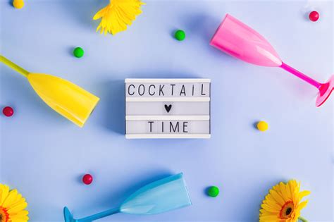 칵테일 타임 비문 밝은 플라스틱 칵테일 안경 멀티 컬러 캔디 드롭 보라색 파란색 배경에 노란색 거베라 꽃이있는 라이트 박스의 상단 보기 플랫 레이 여름 파티 분위기 하이