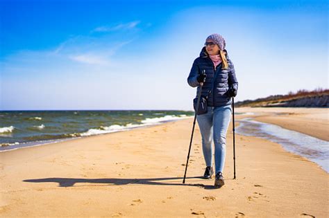 진한 파란색 재킷 청바지 및 겨울 모자를 입고 아름 다운 젊은 여자가 겨울에 화창한 날에 모래 해변을 걷는 북유럽 훈련 앞 View 30 39세에 대한 스톡 사진 및 기타