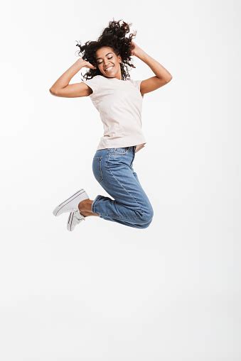 청바지와 티셔츠점프를 입고 흰색 배경에 고립된 완벽한 미소로 기뻐하는 아프로 헤어 스타일을 가진 사랑스러운 미국 여성의 전체 길이 초상화 점프에 대한 스톡 사진 및 기타