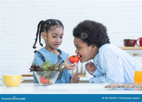 African Little Cute Sister Feeding Smiling Brother Fresh Tomato At Home