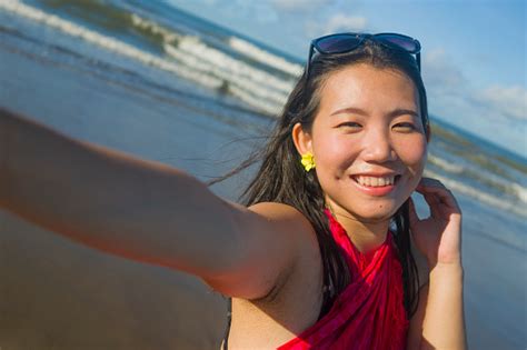 젊은 행복하고 매력적인 아시아 중국 여성 사롱 휴가및 라이프 스타일 개념에서 열대 해변에서 여름 휴가를 즐기는 휴대 전화로 소셜 미디어에 셀카 사진을 찍고 개성 개념에 대한