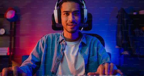 행복한 아시아 남자 게이머는 헤드폰 참여 놀이 비디오 게임 화려한 네온 불빛 컴퓨터 밤 현대 집에서 거실에 있습니다 E스포츠 스트리밍 게임 온라인 가정 격리 활동 개념