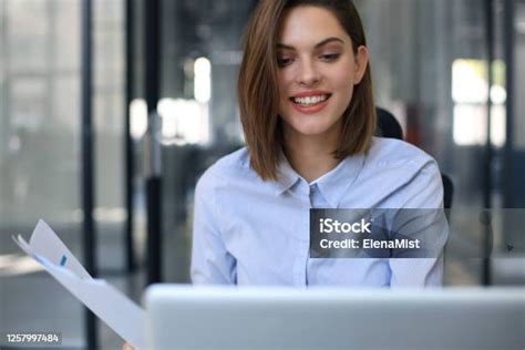 사무실에서 종이 문서를 확인하고 노트북에서 작업하는 매력적인 쾌활한 사업가 경영자에 대한 스톡 사진 및 기타 이미지 경영자 계약서 교육 Istock