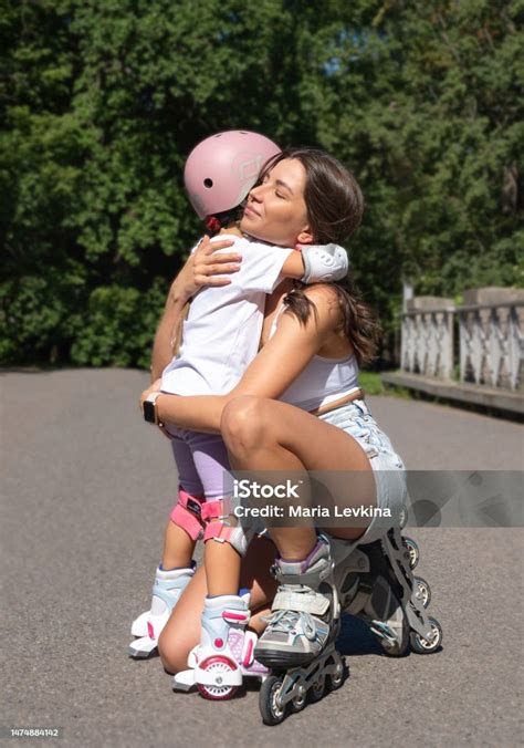 어머니는 여름에 공공 공원에서 인라인 스케이트 롤러에서 스케이트를 타는 어린 딸을 껴안는 것을 가르칩니다 가족 레저 야외 스포츠 활동 게임 네거티브 공간 복사 오솔길에 대한