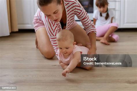 아이들과 함께 부엌에서 바닥에 앉아있는 줄무늬 캐주얼 스타일 셔츠를 입은 젊은 성인 여성 오븐 근처에 앉아있는 노인 아이 기어 다니는 유아 아기와 놀고있는 어머니의 수평