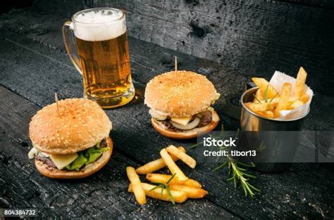 탄 검은 나무 테이블에 맥주와 감자 튀김 햄버거 패스트 푸드 식사입니다 수 제 햄버거는 쇠고기 고기 상 추 토마토 쓰레기통 드레싱 치즈와 향신료로 이루어져 있다 빈티지 감자