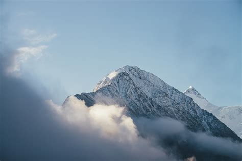 햇빛에 두꺼운 구름 위의 눈 덮인 산의 아름다운 전망 푸른 하늘에 울창한 낮은 구름 사이 흰색 눈 봉우리와 경치 밝은 산 풍경