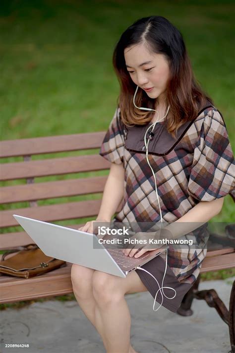 공원에서 노트북으로 작업하고 이어폰을 사용하고 화면에 집중하는 젊은 아시아 여성은 야외에서 현대 원격 근무와 디지털 라이프 스타일을 나타냅니다 Central Florida에