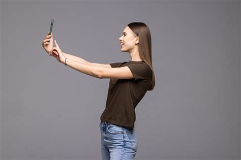 흰색 배경에 고립 된 스마트 폰에서 셀카 사진을 만드는 웃는 여성의 초상화 Brand Name Smart Phone에 대한 스톡