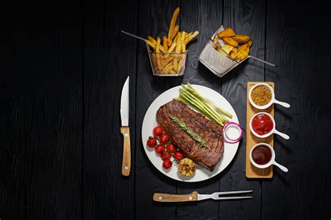 아스파라거스와 토마토 감자 튀김과 시골 감자와 접시에 구운 스테이크 세 가지 소스 케첩 겨자 어두운 나무 배경에 바베큐 상단보기 수평 사진 갈비 음식에 대한 스톡 사진 및