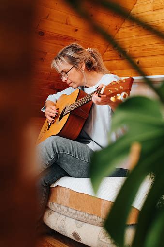 음악 취미와 여가 학습 개념 실내에서 어쿠스틱 기타를 연주하는 백인 중년 여성의 측면 보기 높은 인테리어에 앉아있는 동안 코드를 들고 성인 여성 음악가 45 49세에 대한