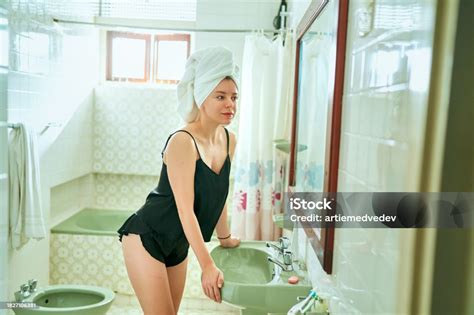 검은 바디 슈트와 머리에 수건을 쓴 젊은 여성이 욕실 아침 일과 가정 환경에서 개인 관리의 싱크대에 기대어 있습니다 가정 생활에 대한 스톡 사진 및 기타 이미지 Istock