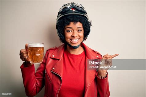 젊은 아프리카계 미국인 Afro 오토바이 여자 와 곱슬 머리 마시는 항아리 의 맥주 매우 행복 가리키는 손과 손가락 으로 측면 가리키기에 대한 스톡 사진 및 기타 이미지