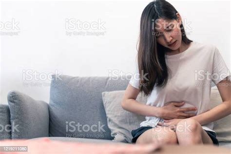 식중독으로 아픈 아시아 젊은 여성 그녀는 집에서 소파에 앉아있다 여성은 경련을 통해 복통과 곱슬 머리가있다 소녀는 너무 고통스럽고 슬프고 외로워합니다 헬스케어 식품 및 의료