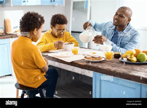 Cheerful young father talking with sons while pouring milk Stock Photo ...