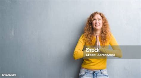 구걸 하 고 손으로 얼굴 매우 감정적이 고 걱정에 희망 식 함께 기도 회색 그런 지 벽에 빨강 머리 젊은 여자 용 서에 대 한 요구 종교 개념입니다 벽에 대한 스톡 사진 및