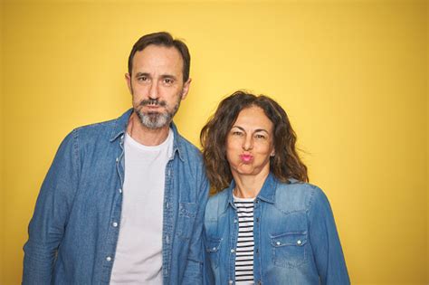 아름 다운 중년 부부는 함께 재미 있는 얼굴과 고립 된 노란색 배경 퍼핑 뺨 위에 데님 셔츠를 입고 공기 미친 표정으로 입이 팽창 2명에 대한 스톡 사진 및 기타 이미지