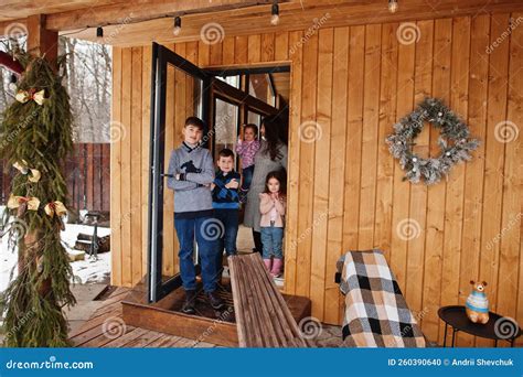 Madre E Hijos En Casa De Madera Moderna Parados Cerca De La Entrada De La Puerta Foto De Archivo