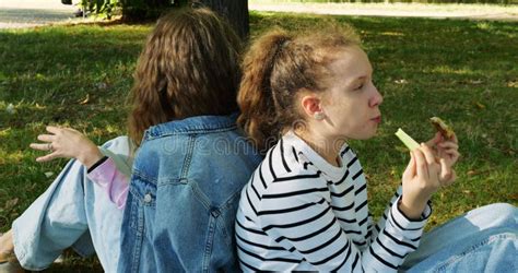 Girl Eats With Open Mouth Holding Cucumber Mid Bite While Friend Stays