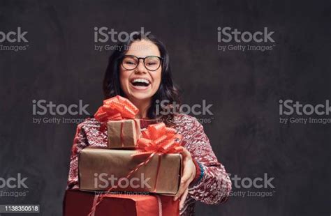 어두운 질감의 배경에 고립 된 선물 상자를 들고 안경 및 따뜻한 스웨터를 입고 행복 한 갈색 머리 소녀의 초상화 갈색 머리에