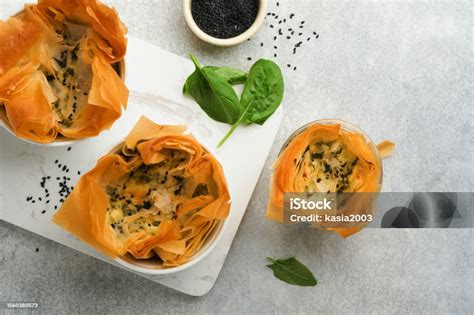 부드러운 페타 치즈와 시금치를 곁들인 필로 파이는 오래된 회색 테이블 배경에 세라믹 몰드에 담겨 있다 필로 부분 파이 작은 구운