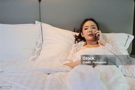 하얀 잠옷을 입은 젊고 아름다운 아시아 여성이 잠자리에 들기 전에 모바일 스마트폰이 있는 침실에 누워 좋은 꿈을 꾸고 있다 라이프스타일 컨셉 취침시간에 대한 스톡 사진 및