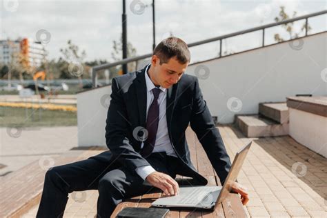 Мужчина в деловом костюме и с ноутбуком сидит на скамейке бизнесмен с ноутбуком Ozero