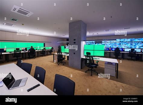 Group Of Security Data Center Operators Working In A CCTV Monitoring Room Looking On Multiple