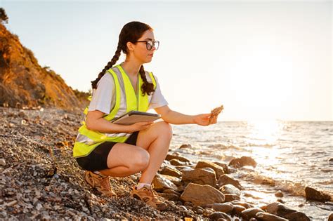 조끼를 입고 해변 토양을 분석하는 전자 태블릿을 들고 있는 젊은 자원 봉사자 여성 배경에는 바다 해안 일몰이 있습니다 공간을 복사합니다 해양 오염의 개념 25 29세에 대한