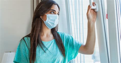 자택 격리 백인 여성은 의료용 마스크를 쓰고 창문에 앉아 밖을 내다보며 외출하고 싶어합니다 코로나 바이러스 감염 전염병 질병 발생 및 전염병으로부터 보호합니다 사진