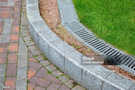 돌 벽돌 타일의 보행자 포장을 따라 화강암 연석에서 녹색 잔디 잔디와 돌 자갈이 있는 보도 쪽의 철 배수 창살 아무도 없습니다 Runoff Election에 대한 스톡 사진