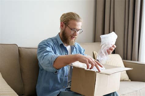 해피 맨 고객 언패킹 골판지 상자 는 오픈 포스트 메일 배달 패키지를 받을 수 있습니다 미소 젊은 만족 쇼핑객 언 박싱 소포 언 팩 배송 주문 제품 구매 집에서 소파에 앉아