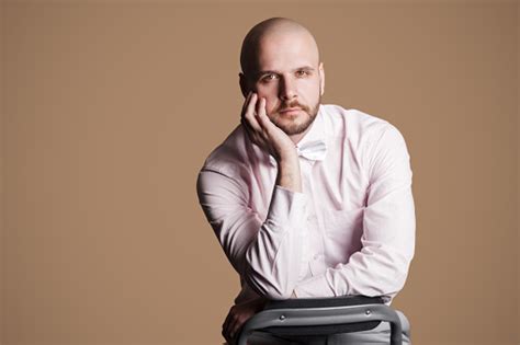 밝은 분홍색 셔츠와 흰색 나비의 자에 앉아 하 고 턱에 손으로 카메라를 보고 심각한 잘생긴 수염된 대머리 남자의 초상화 40