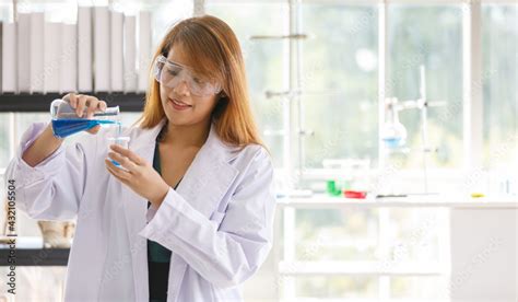 Asian Babe Successful Female Scientist In White Lab Coat And Safety Goggles Pouring Blue