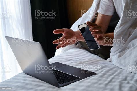 한 남자가 집이나 호텔에서 침대에서 노트북과 스마트폰으로 작업합니다 원격 작업 집에서 사무실 침실에 있는 남자가 노트북에 타이핑 학생들을위한 거리 학습 인터넷 서핑