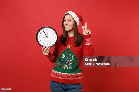 산타 소녀에 고립 된 밝은 빨간색 배경 위로 검지 손가락을 가리키는 둥근 시계를 들고 웃 고 시간이 촉박 합니다 행복 한 새 해 2019 축 하 휴일 파티 개념입니다 복사